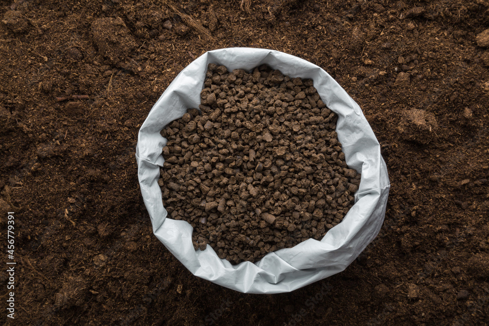 Opened plastic bag with black granules of chicken manure on dark soil ...