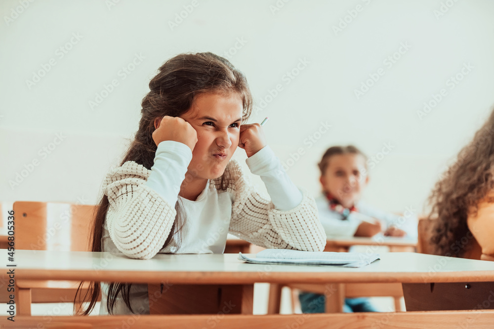 An angry face of a little girl sitting in a school desk.Selective focus ...