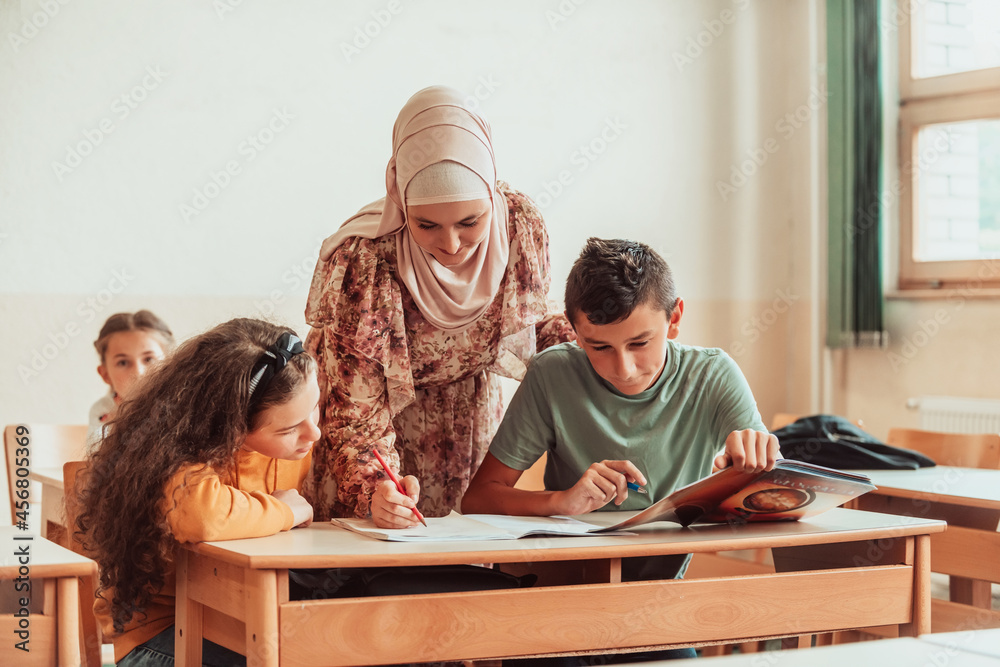 Female hijab muslim teacher helps school kids to finish they lesson ...