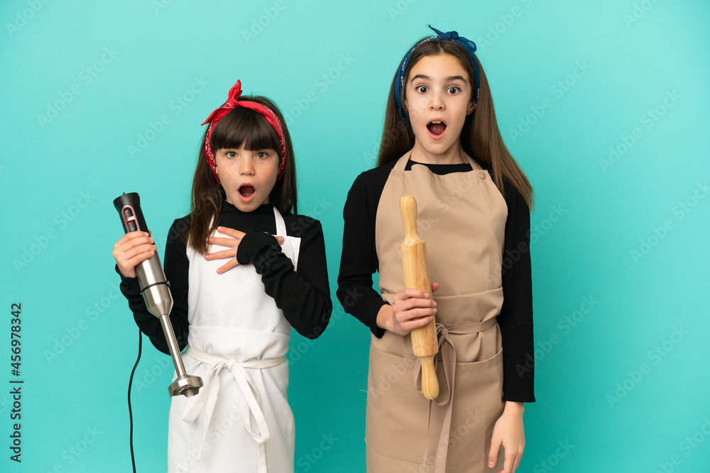 Little sisters cooking at home isolated on blue background with ...