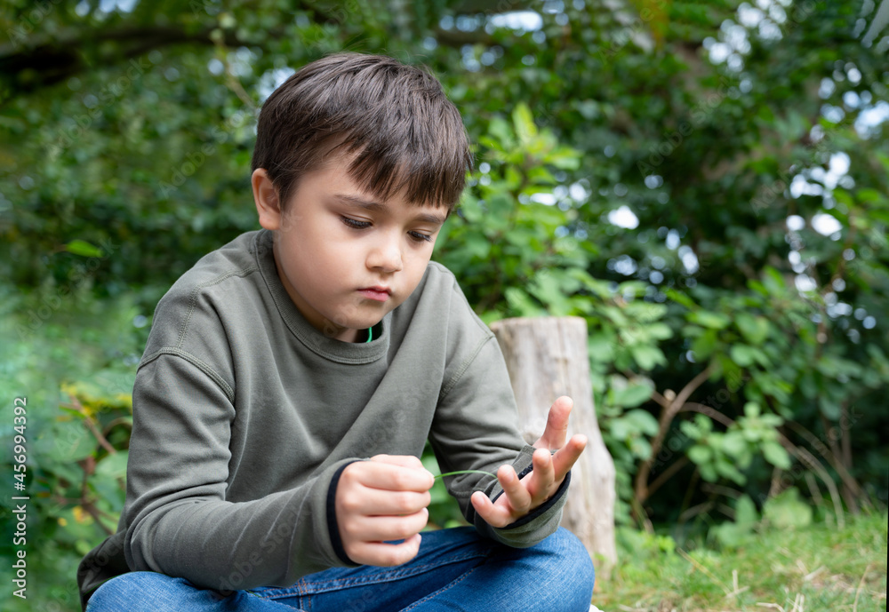 Emotional portrait of Lonely kid sitting alone on grass in the garden ...