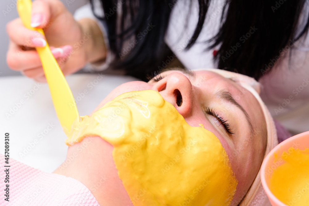 Applying a golden mask on the face after the cleansing procedure, an ...