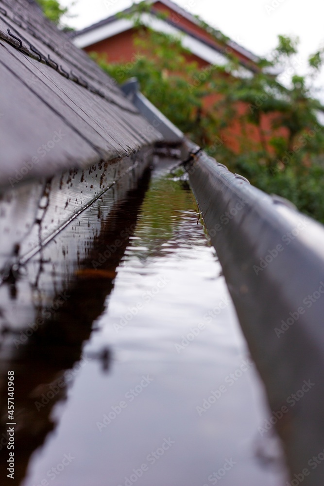 A portrait of a clogged roof gutter full of rain water during a rainy ...