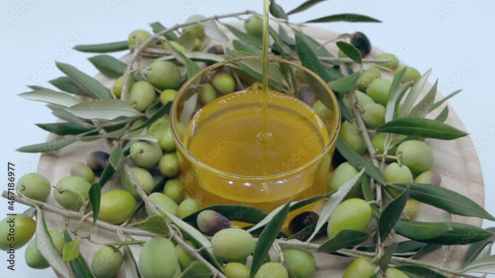 Organic olive oil pouring into crystal bowl rotating on wooden board ...