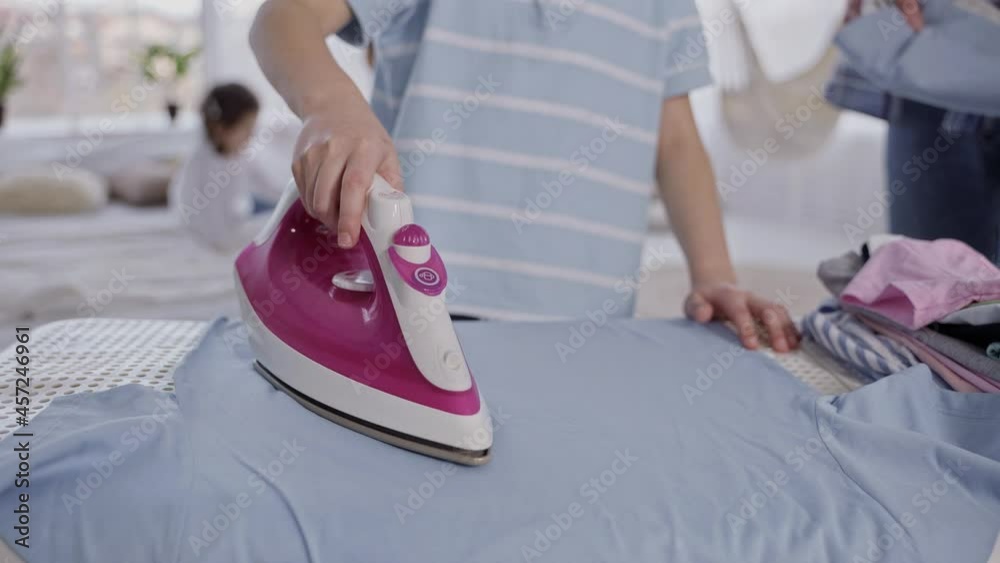 Cheerful preteen boy ironing T-shirt on his own, close-up of iron in ...