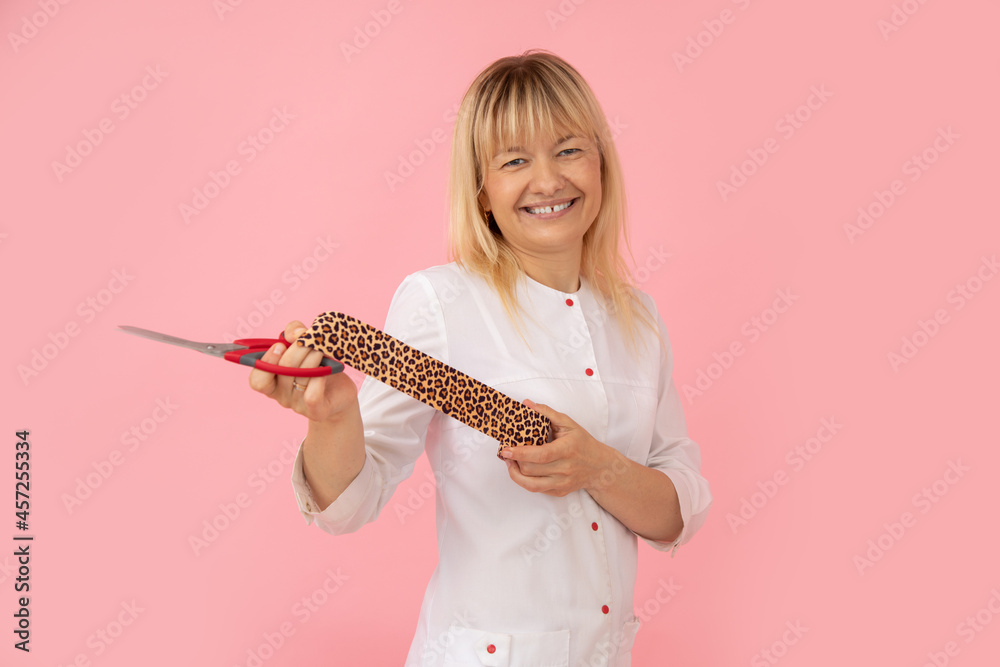 Foto de Blonde cosmetologist in white medical uniform shows how to cut ...