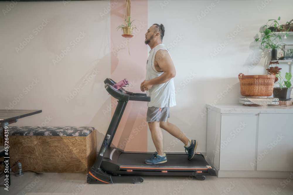 Profile shot of a bearded matured man running on a treadmill at home ...