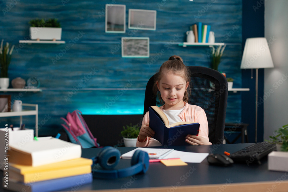 Little caucasian student holding book reading pages for school work ...