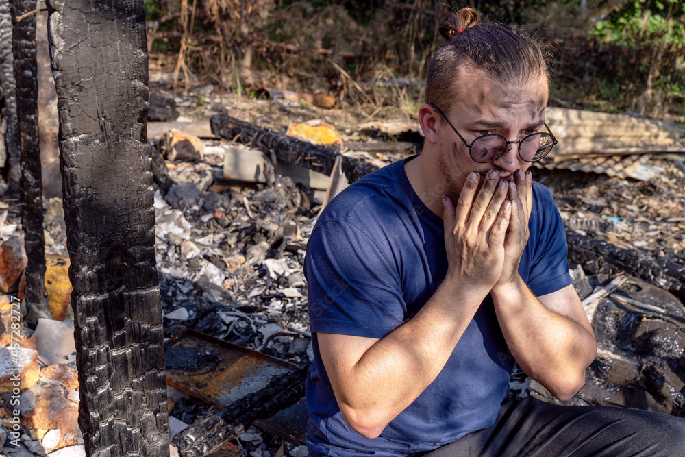 Young man sits on the ruins of house destroyed with fire. Damaged ...
