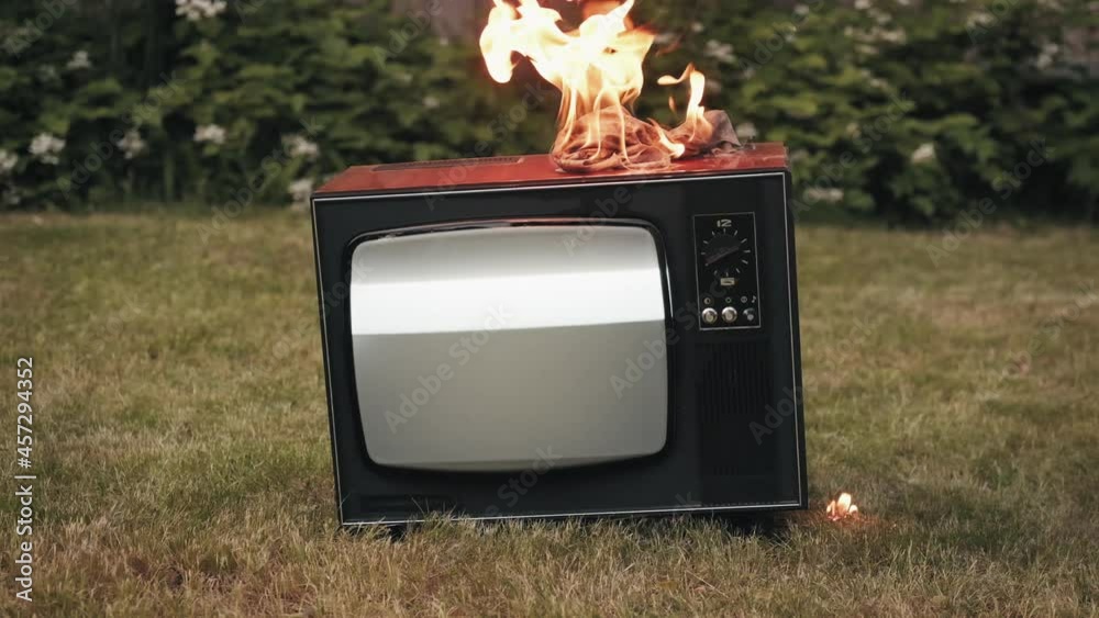 Man sets fire to an old retro TV by throwing a burning rag at it. There ...