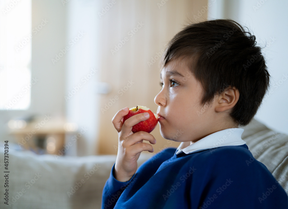 Mixed race child eating red apple while watching TV, Side view portrait ...