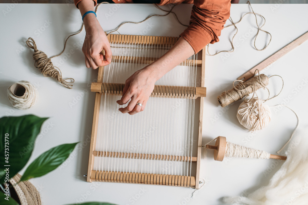 Hands of woman weaving wool rug at the table with flowers and threads ...