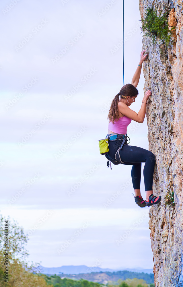 Vertical profile photo of a young woman climbing a steep rock wall ...