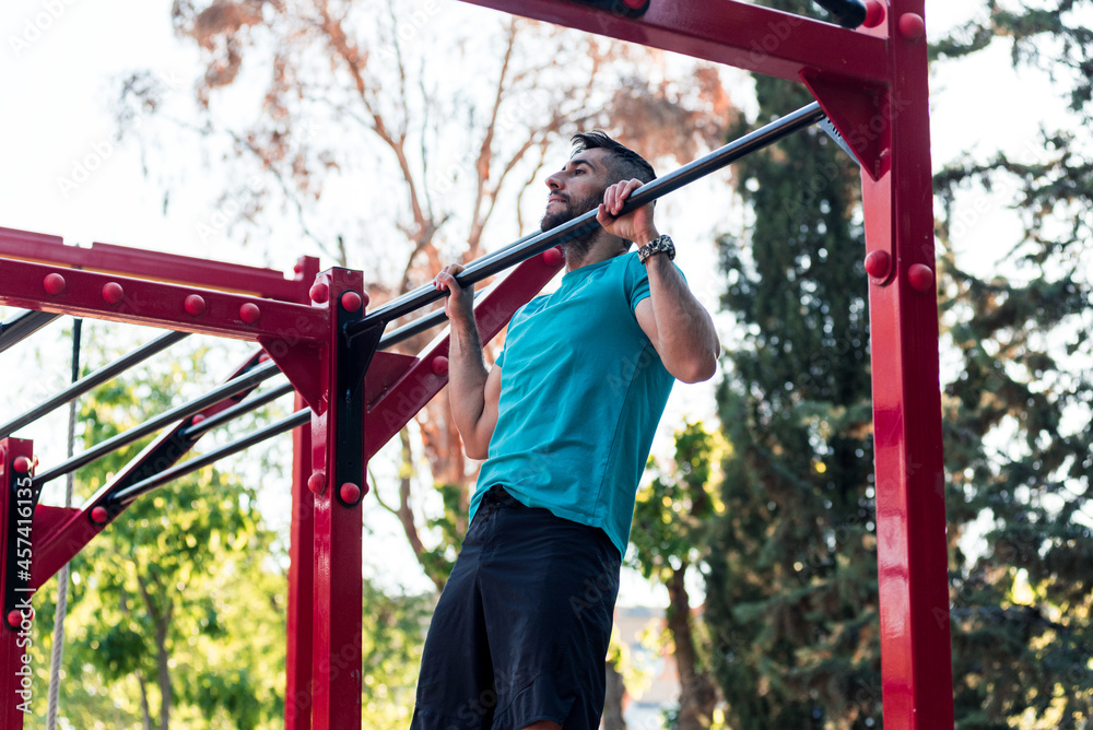 Dark-haired athlete with beard doing a pull-up on a calisthenics bar ...