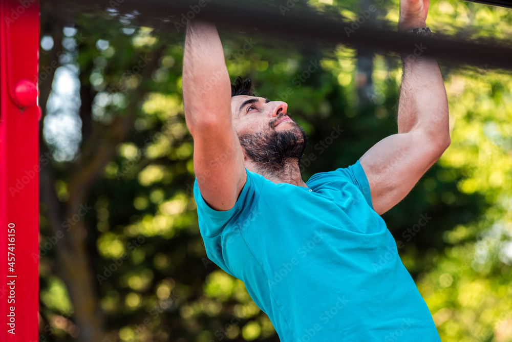 Dark-haired athlete with beard doing a pull-up on a calisthenics bar ...