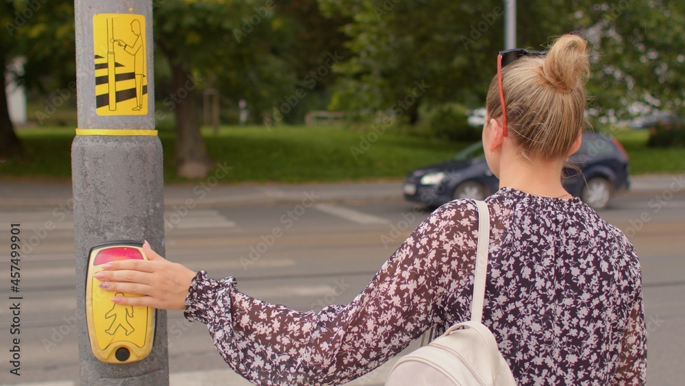 Female pedestrian presses a traffic light button to cross the road. The ...