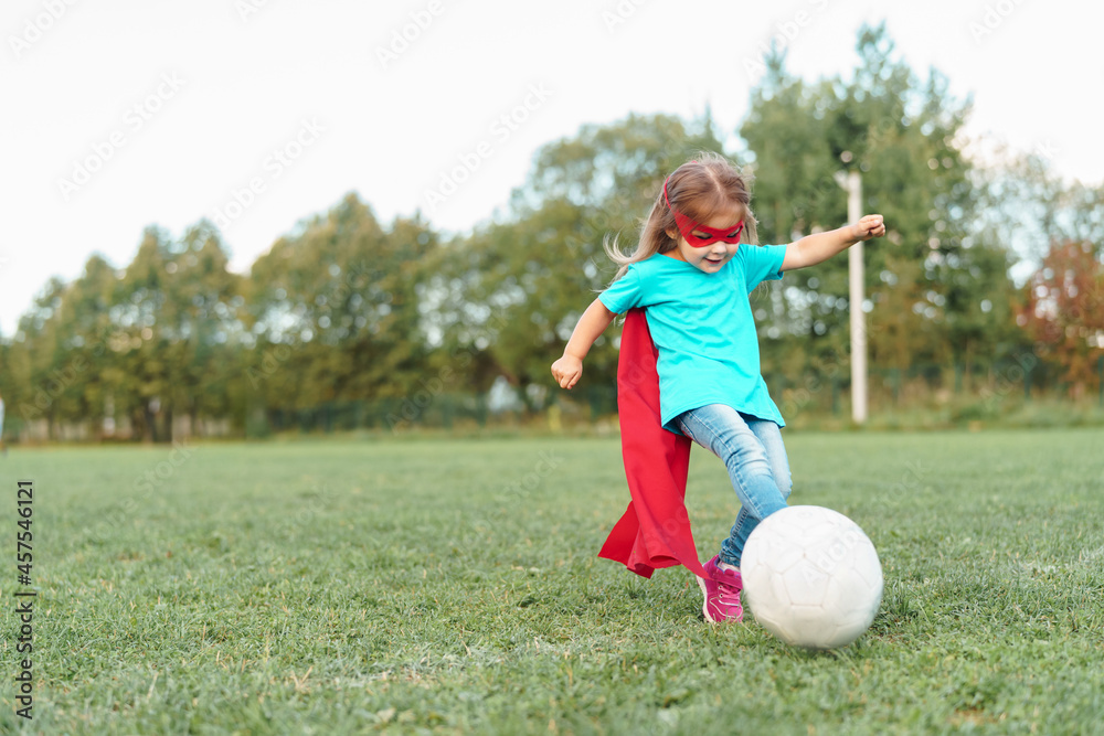 little girl child in a superhero costume is playing football in the ...