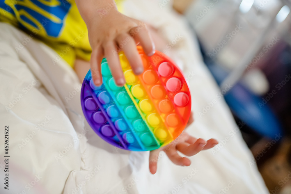 hands of toddler child are holding round pop it. A cheerful child on ...
