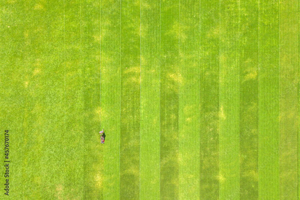 Aerial view of small figure of man worker trimming green grass with ...