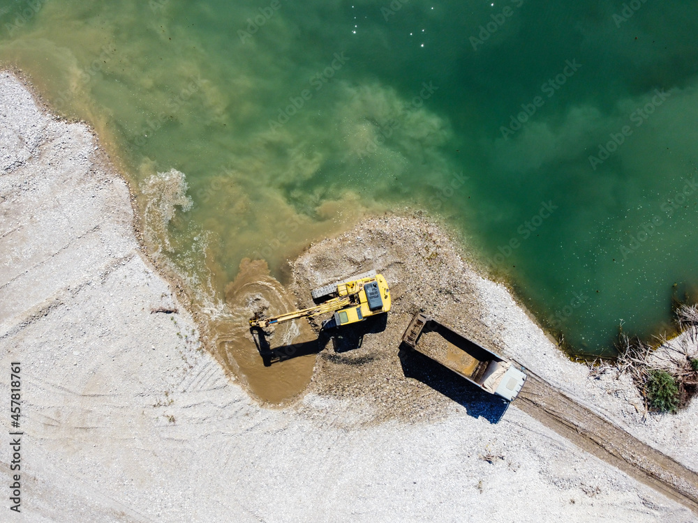 Excavator digging and loading sand into dump truck at river bank. Heavy ...