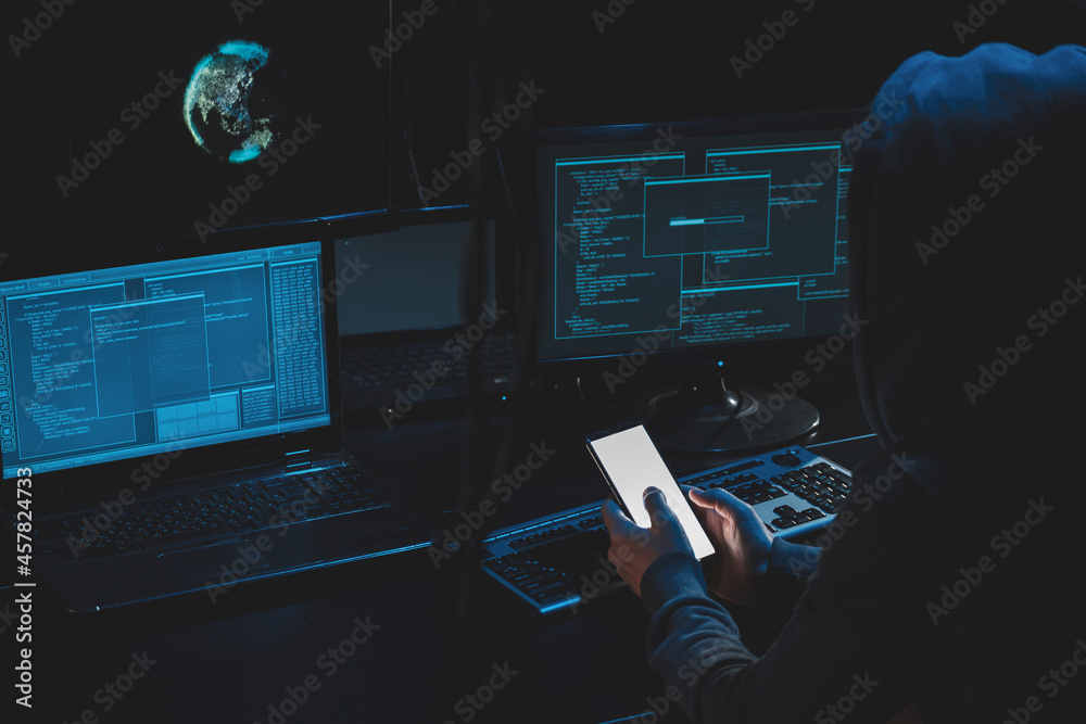 Overhead hacker in hood working at laptop and mobile phone typing text ...