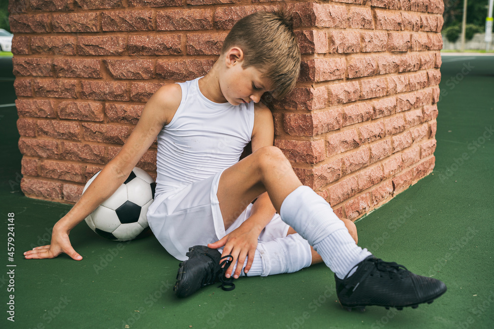 Exhausted young soccer boy leans against wall to rest after playing ...