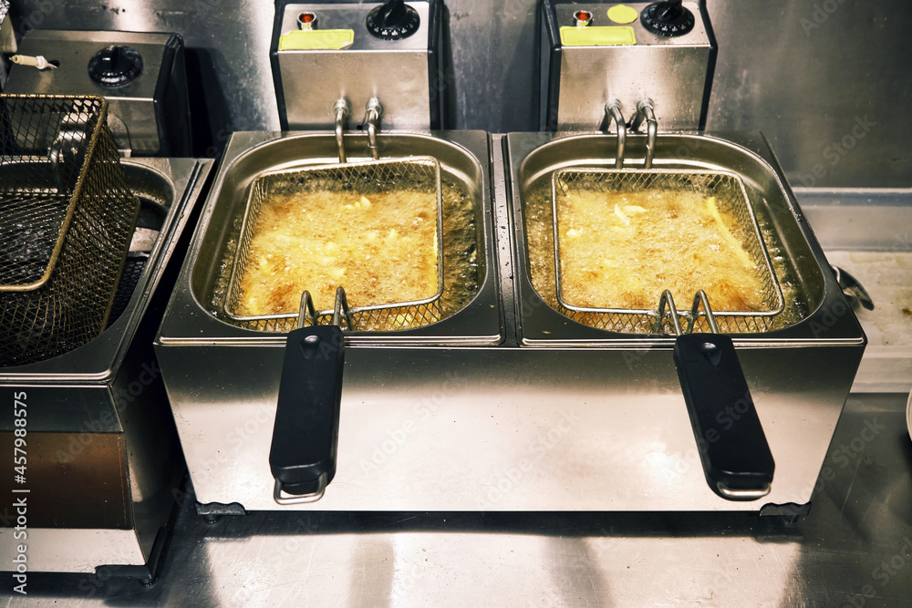 French fries potatoes frying in the hot fryer of a restaurant kitchen ...