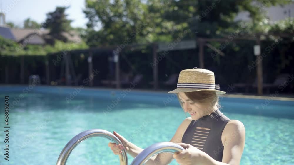Beautiful young woman enters the pool, holding the pool ladder ...