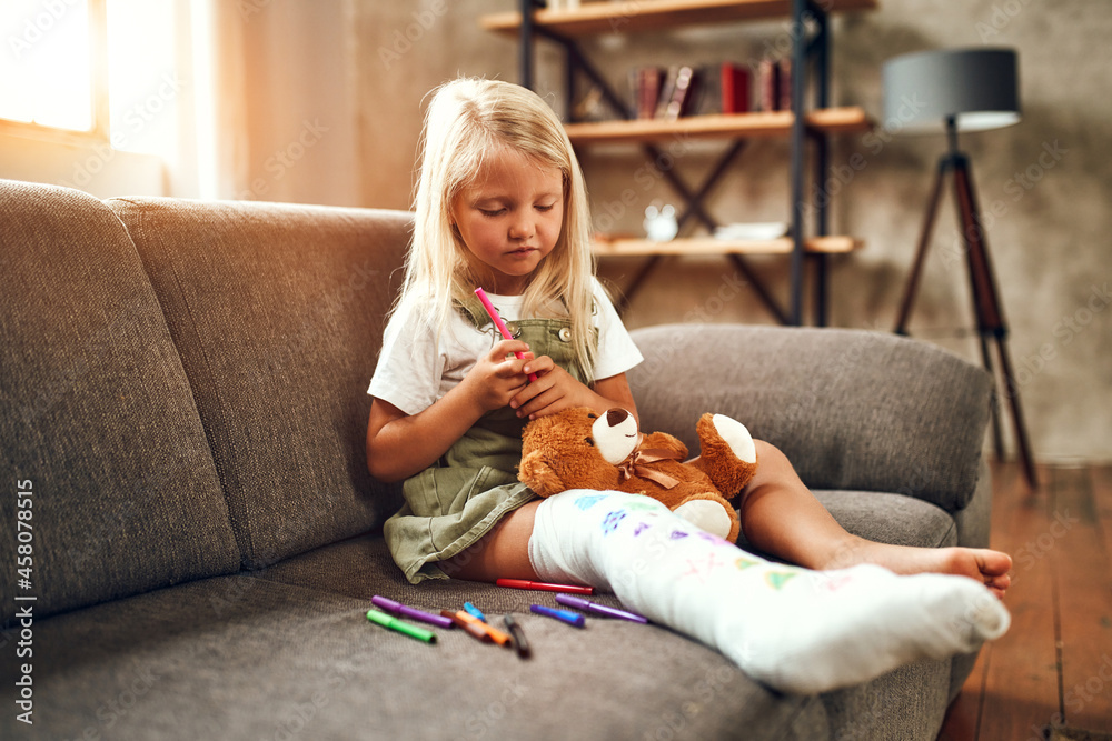 Little girl with a broken leg on the couch. The child draws with felt ...