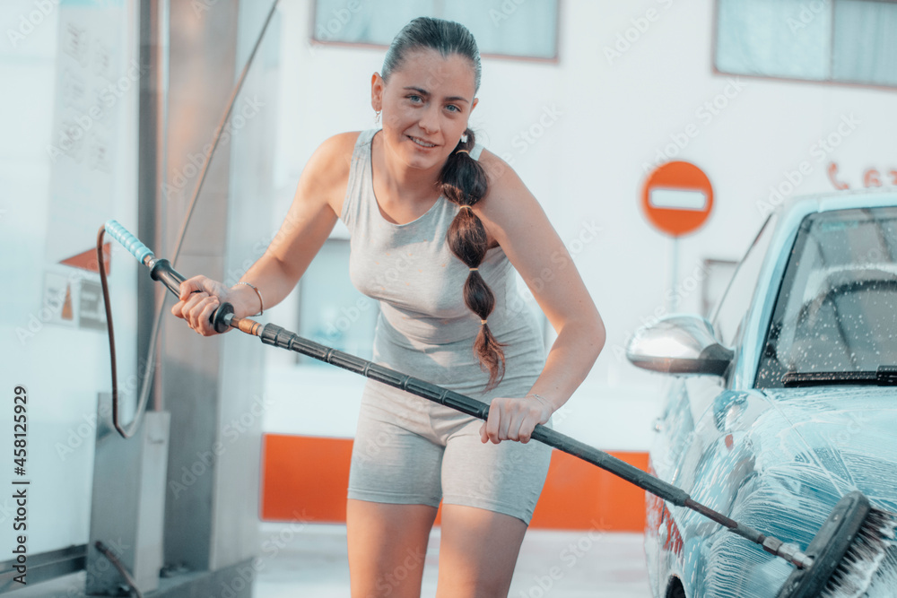 Chica joven empleada de un lavadero de coches fregando la carrocería ...