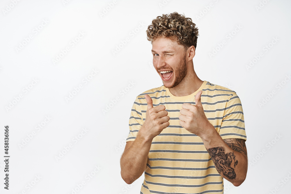 Handsome blond man winks and shows thumbs up in approval, praise you ...