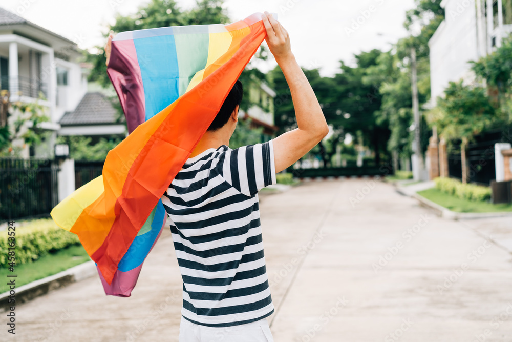 Rear view of a young man holding and waving the rainbow flag in support ...