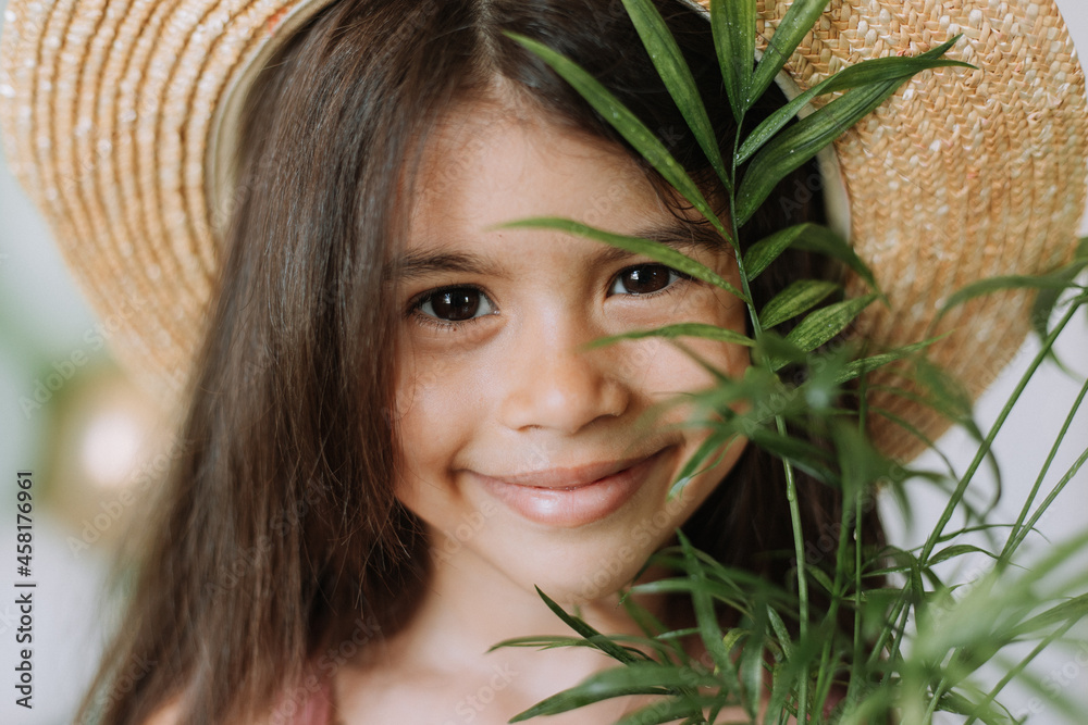 Face of a little girl surrounded by tropical leaves. Closeup portrait ...