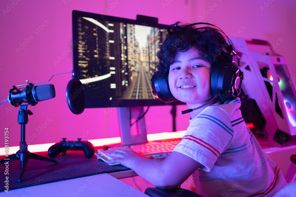 Cute curly-haired little Asian boy gamer in headphones sitting playing ...