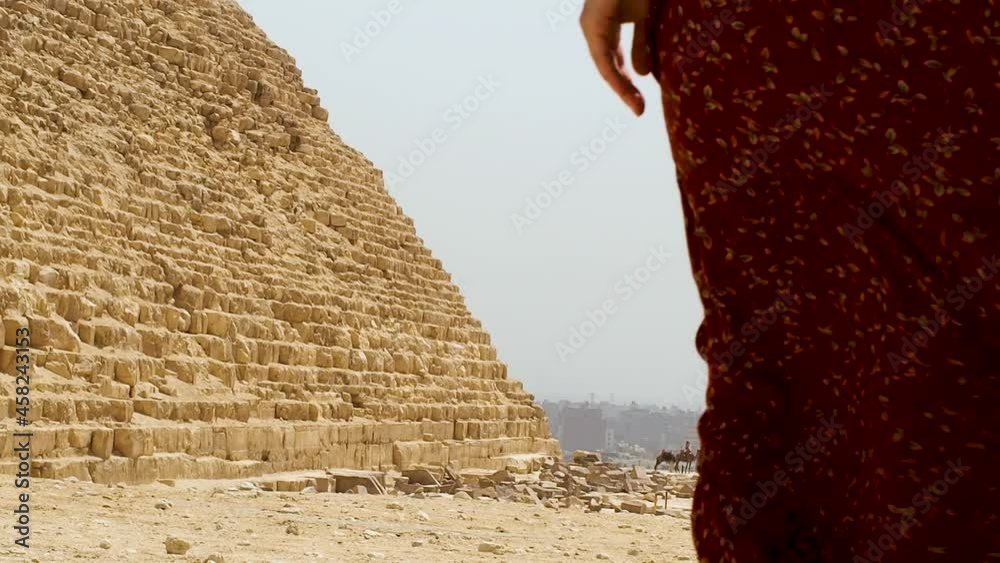 A woman walks towards the pyramid of Khafre in a red dress with a hood ...