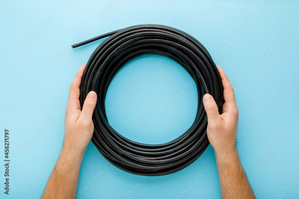 Young adult man hands holding black rolled cable on light blue table ...