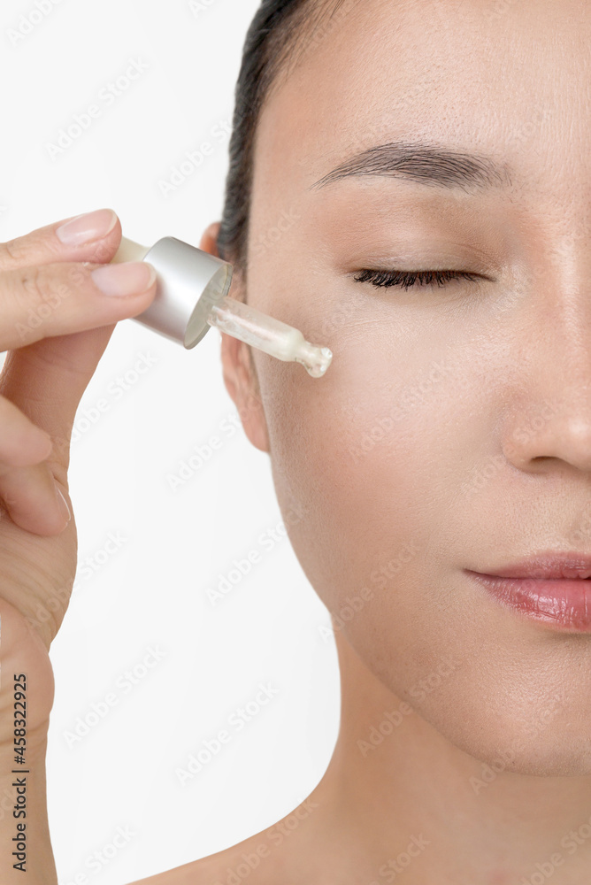 Beautiful young Asian woman apply oil on the face close-up. half of the ...