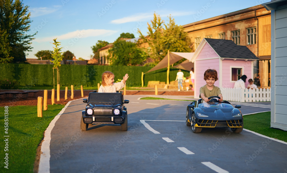 happy kids driving the toy electric cars, having fun on playground ...