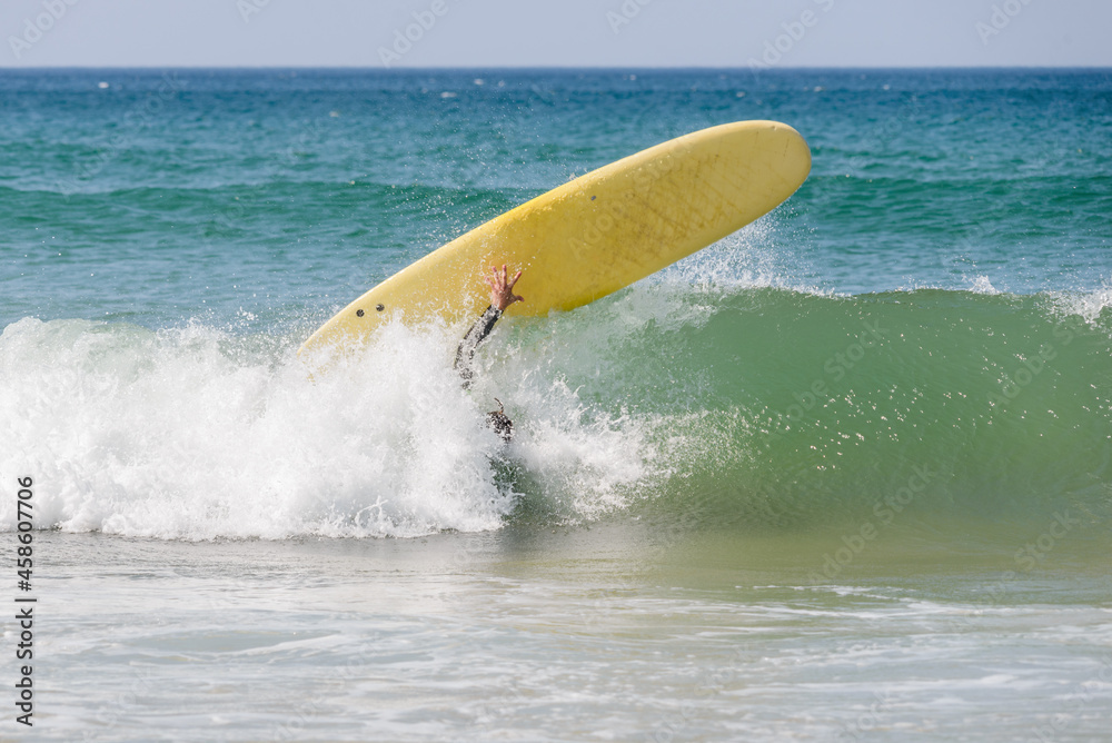 Surfer dangerously falls of his yellow soft top surfboard. Stock Photo ...