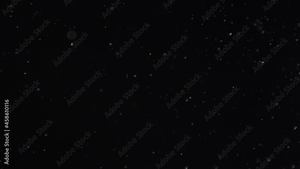 A suspension of white-silver particles in the air on a black background. Some of the particles ...