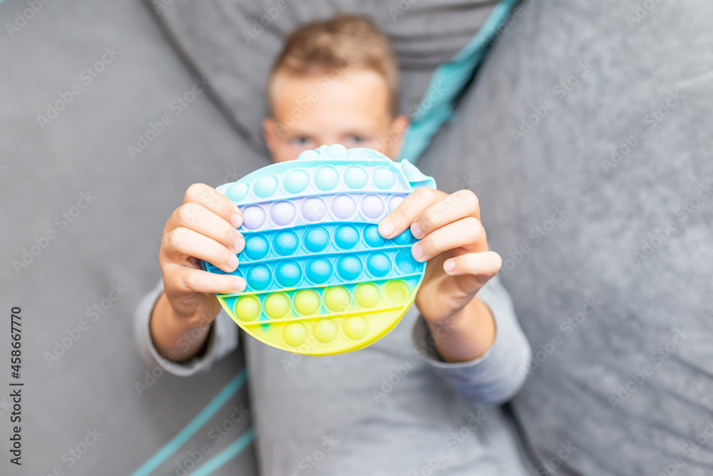 Schoolboy 10s boy lying on the couch and playing with sensory pop it ...