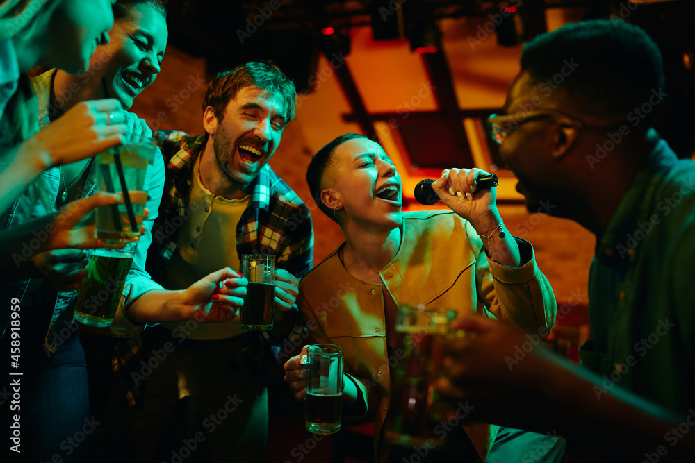 Foto de Cheerful friends having fun while singing karaoke during their ...
