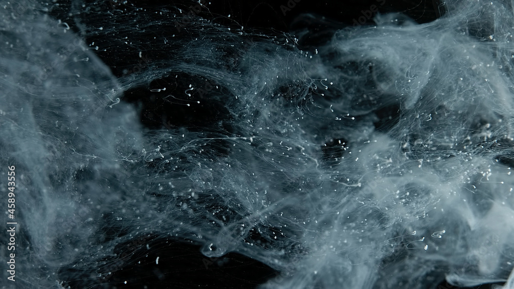 White cloud of ink on a black background. Drops of white ink in water ...
