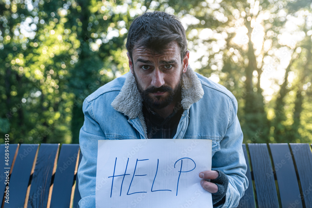 Young sad sick poor man sitting on the bench on the street holding help ...