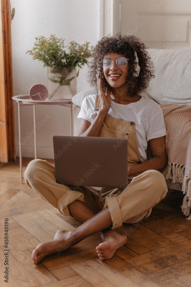 gorgeous dark-skinned girl works at home using laptop while sitting on ...