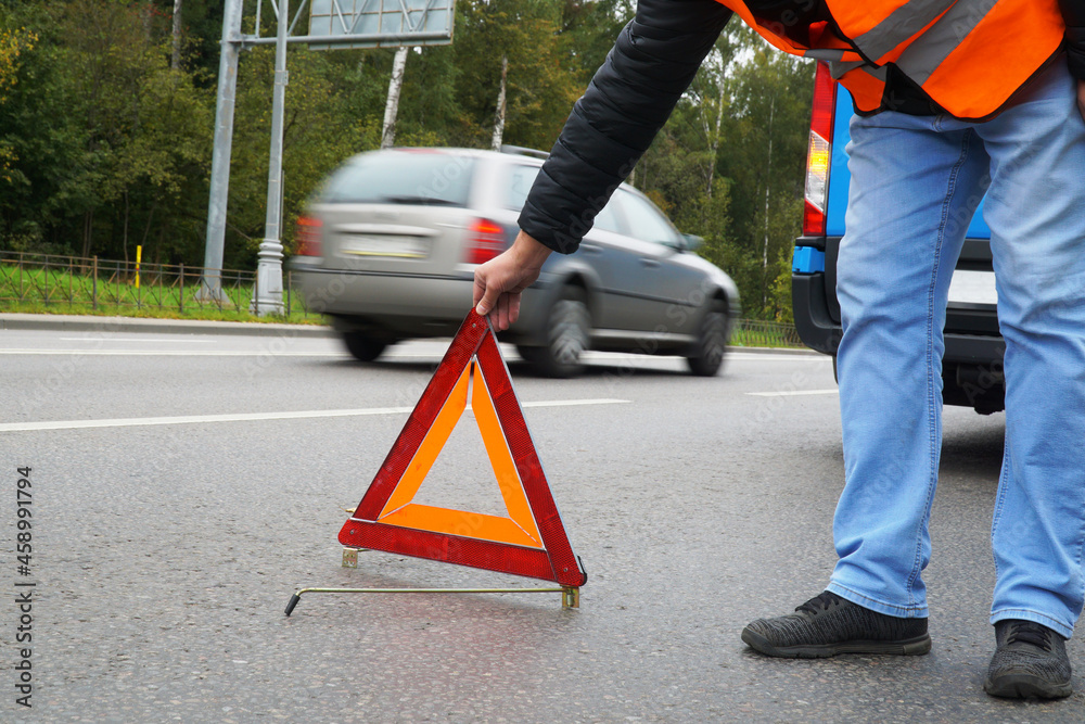 A man in an orange vest places an emergency stop sign on the road in ...