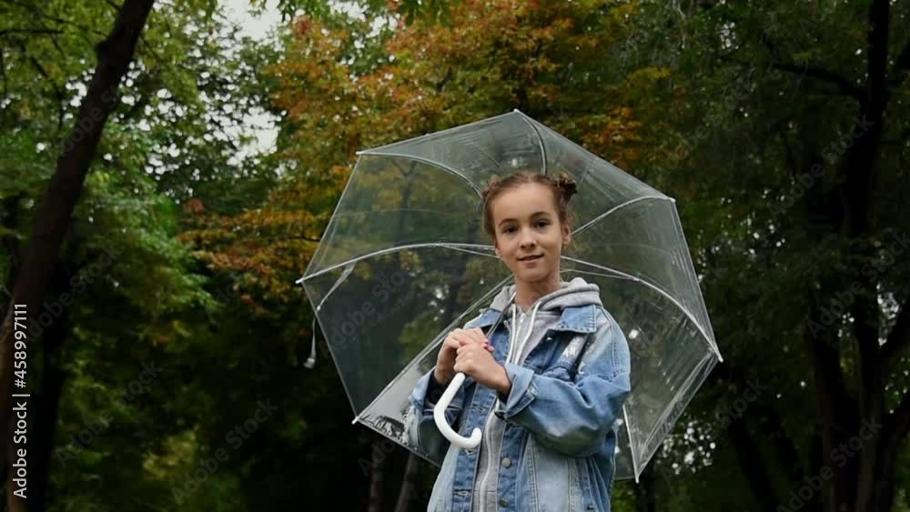 A girl walks and plays with a transparent umbrella in the park. Smiling ...