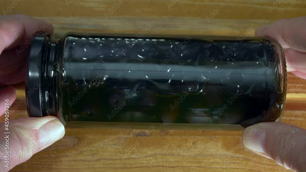 Closeup POV overhead shot of a man’s hands shaking a new jar of Spanish ...