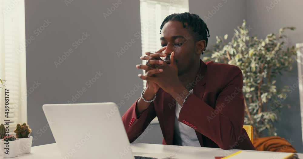 Handsome dark-skinned guy leans against desk with hands bent over ...