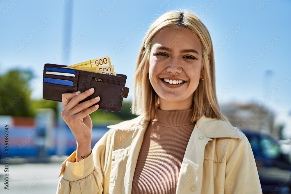 Young blonde girl smiling happy holding wallet with norway krone ...